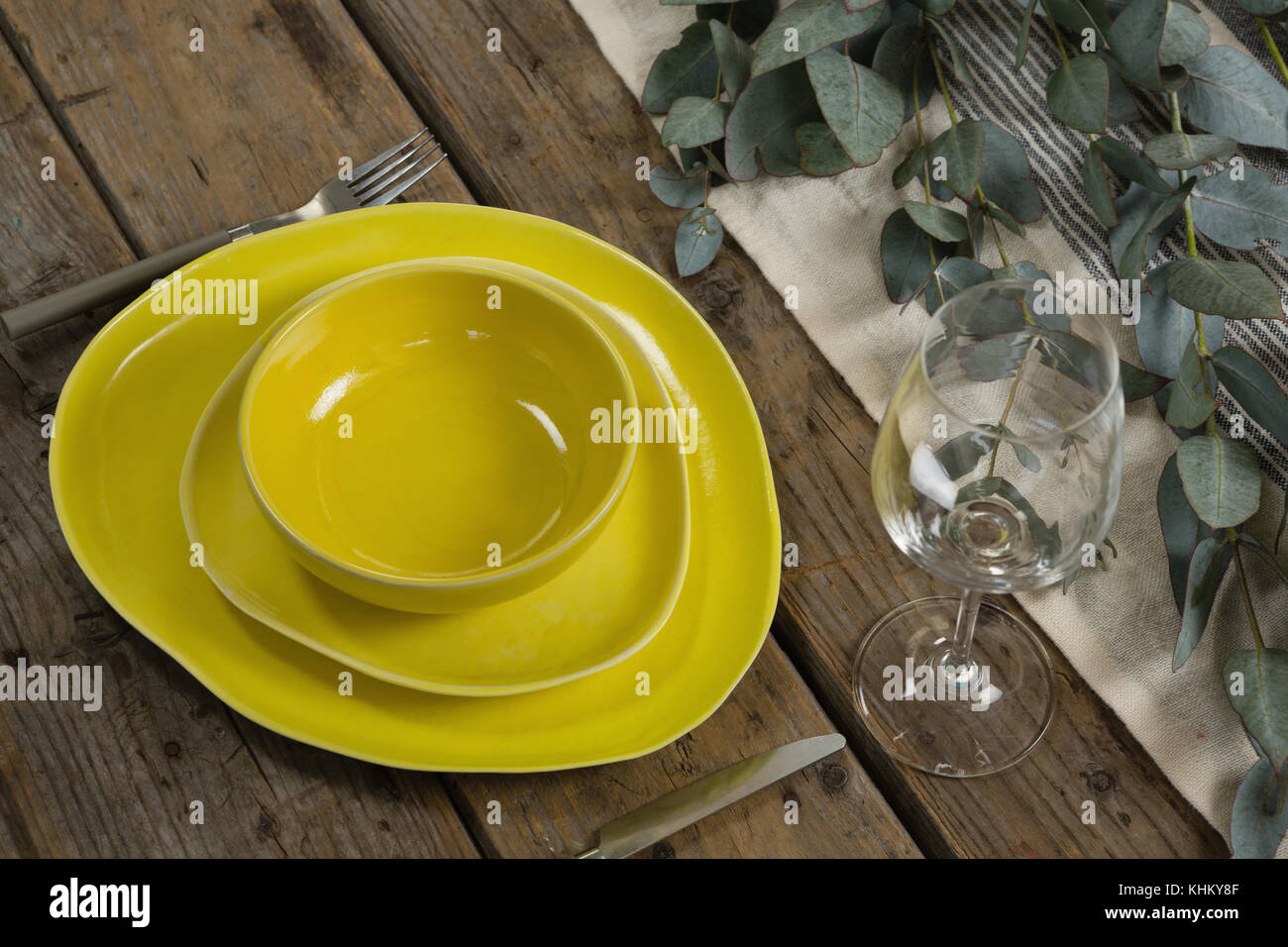 Stack of various dinnerware with cutlery and empty glass on wooden ...