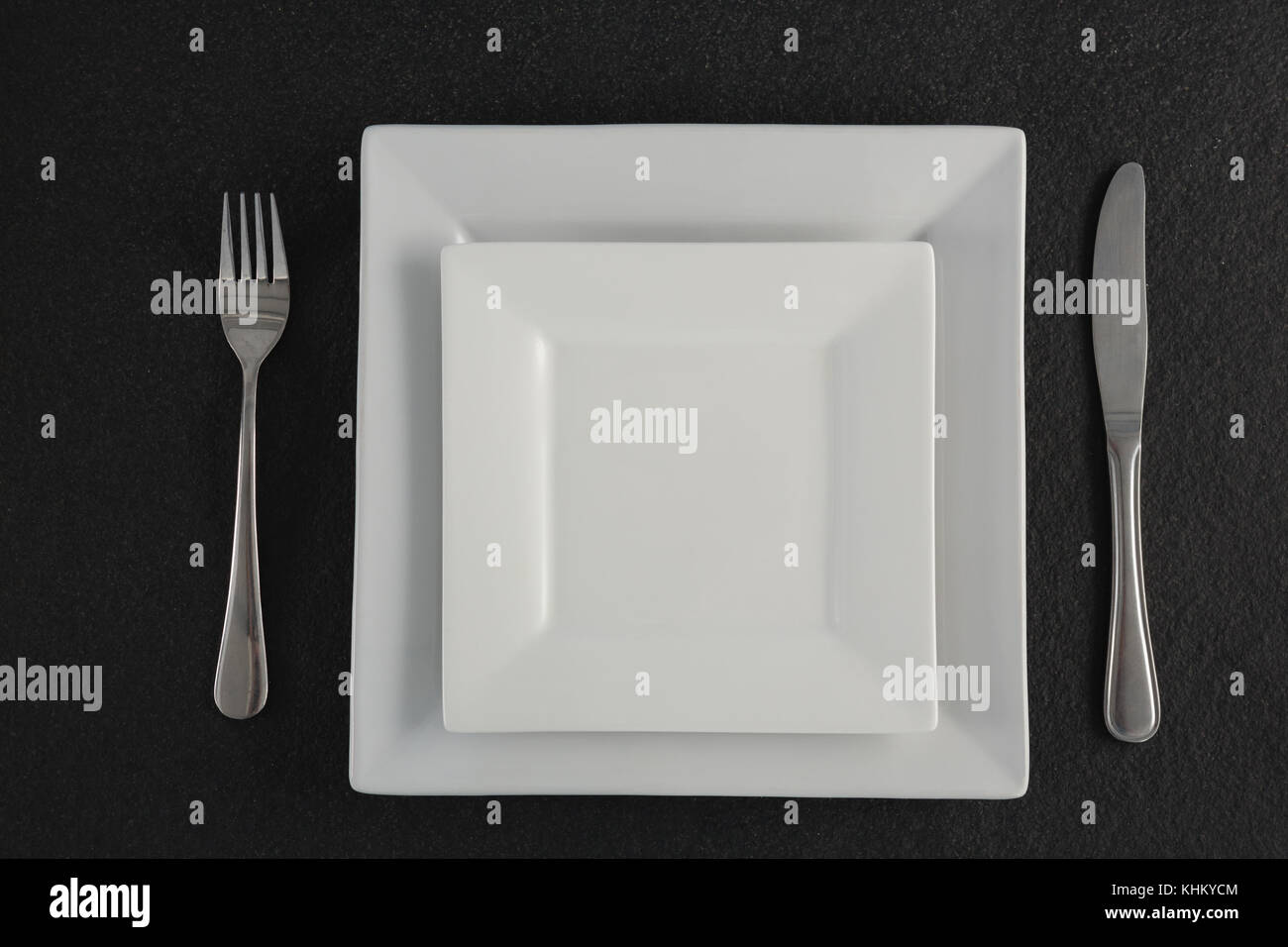Close-up of square plates and cutlery set on a table Stock Photo - Alamy