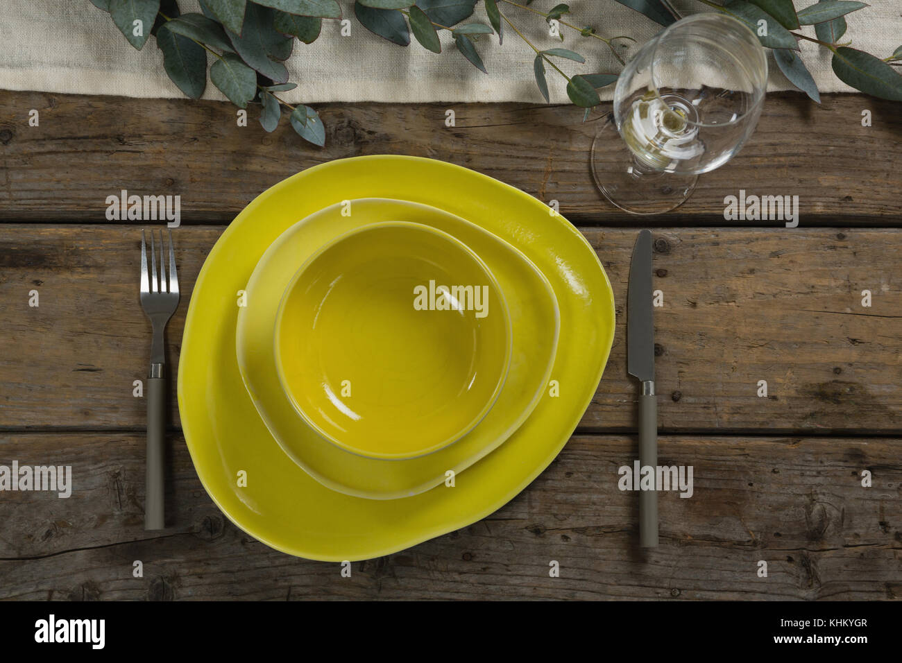 Stack of various dinnerware with cutlery and empty glass on wooden ...