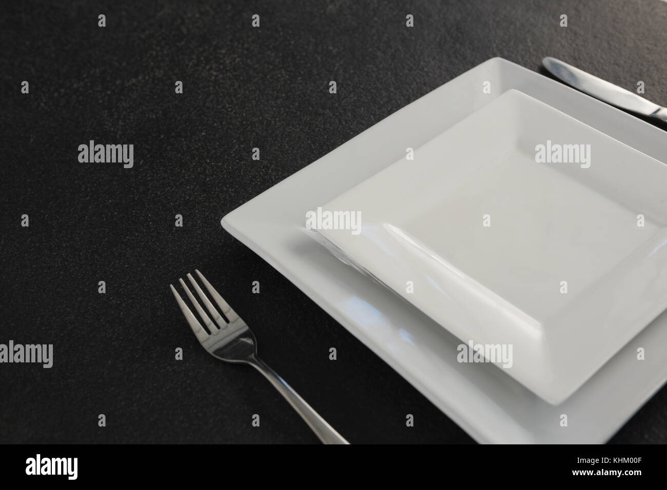 Close-up of square plates and cutlery set on a table Stock Photo - Alamy