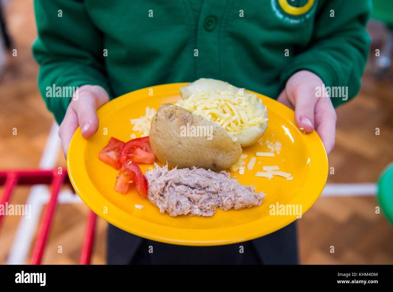 A child holding a school dinner of baked potato, tuna, tomato and ...