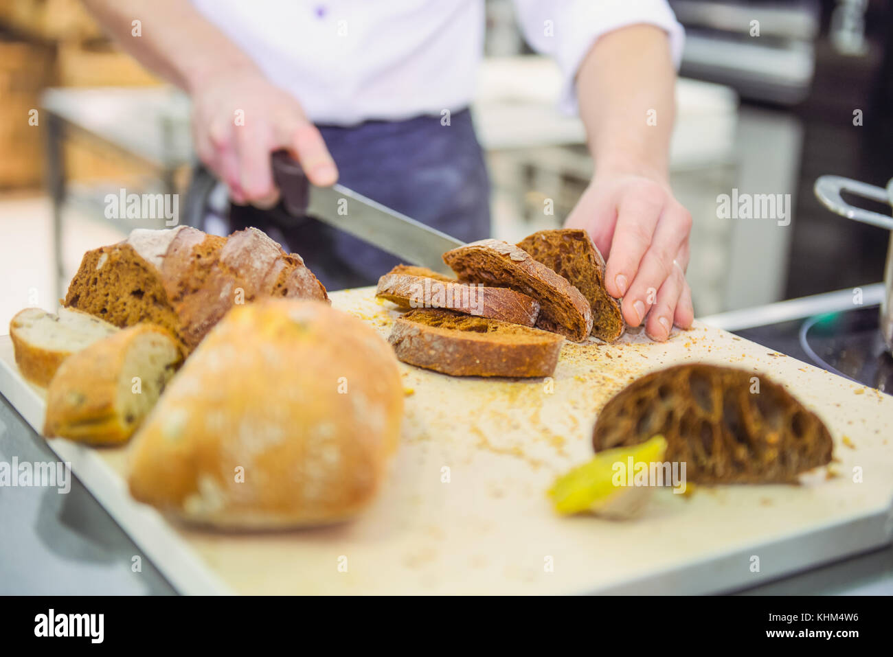 A male chef's hand cutting whole grain bread with knife on the table ...