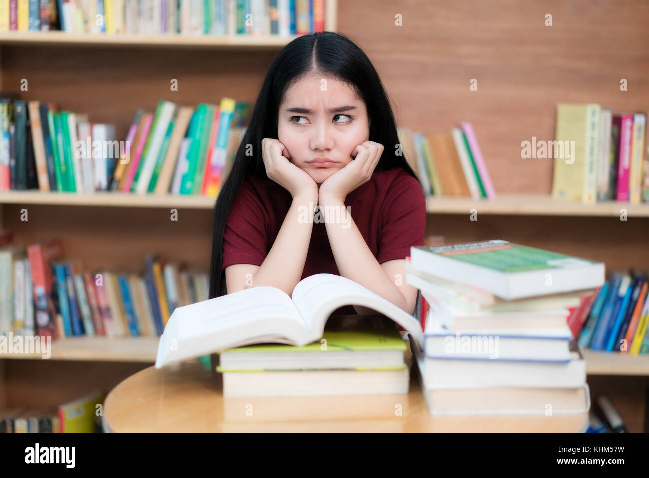 Asian woman student boring reading book at library with a lot of books ...