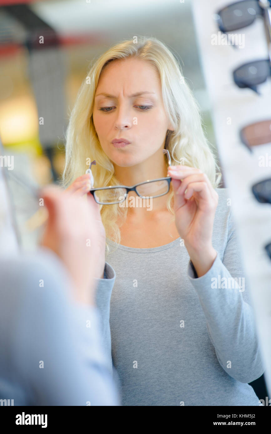portrait of unsure female customer trying spectacles in optical store ...