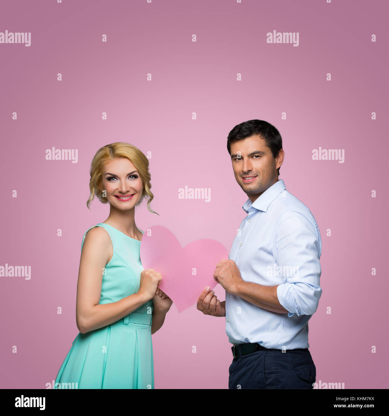 Beautiful young couple holding big pink hearts. Blond woman in mint ...