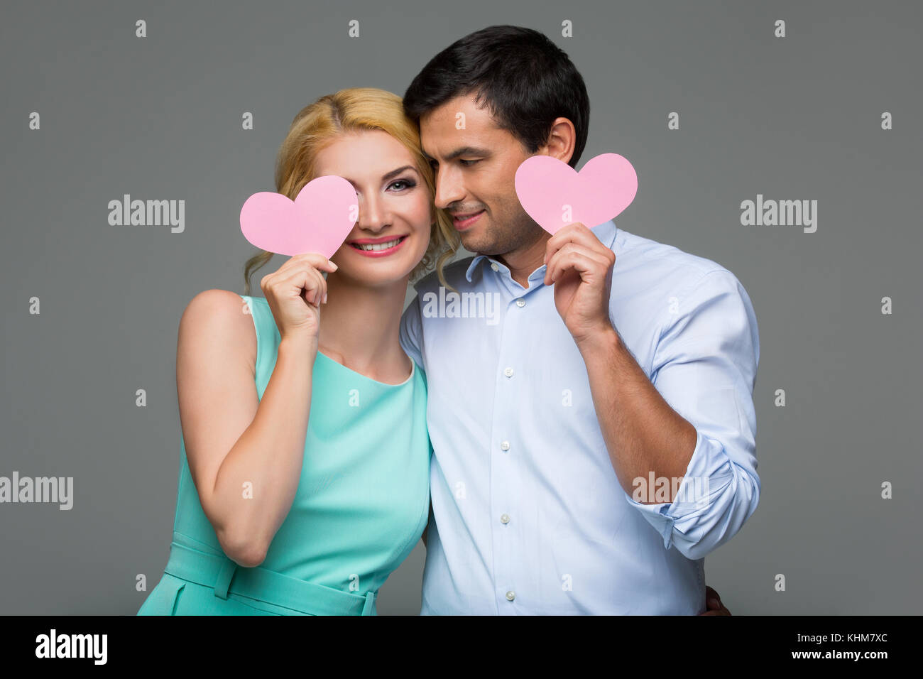 Beautiful young couple holding big pink hearts. Blond woman in mint ...