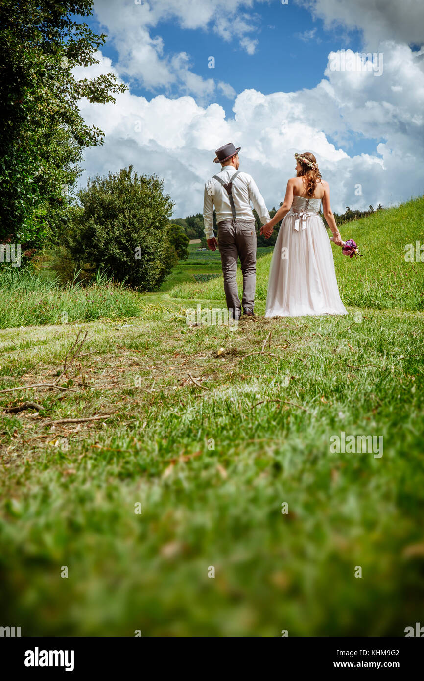 Photo of a young newlywed couple walking down a path through a park ...