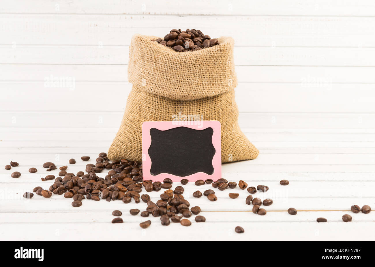 Jute bag of roasted coffee with small chalkboard on white wooden table ...