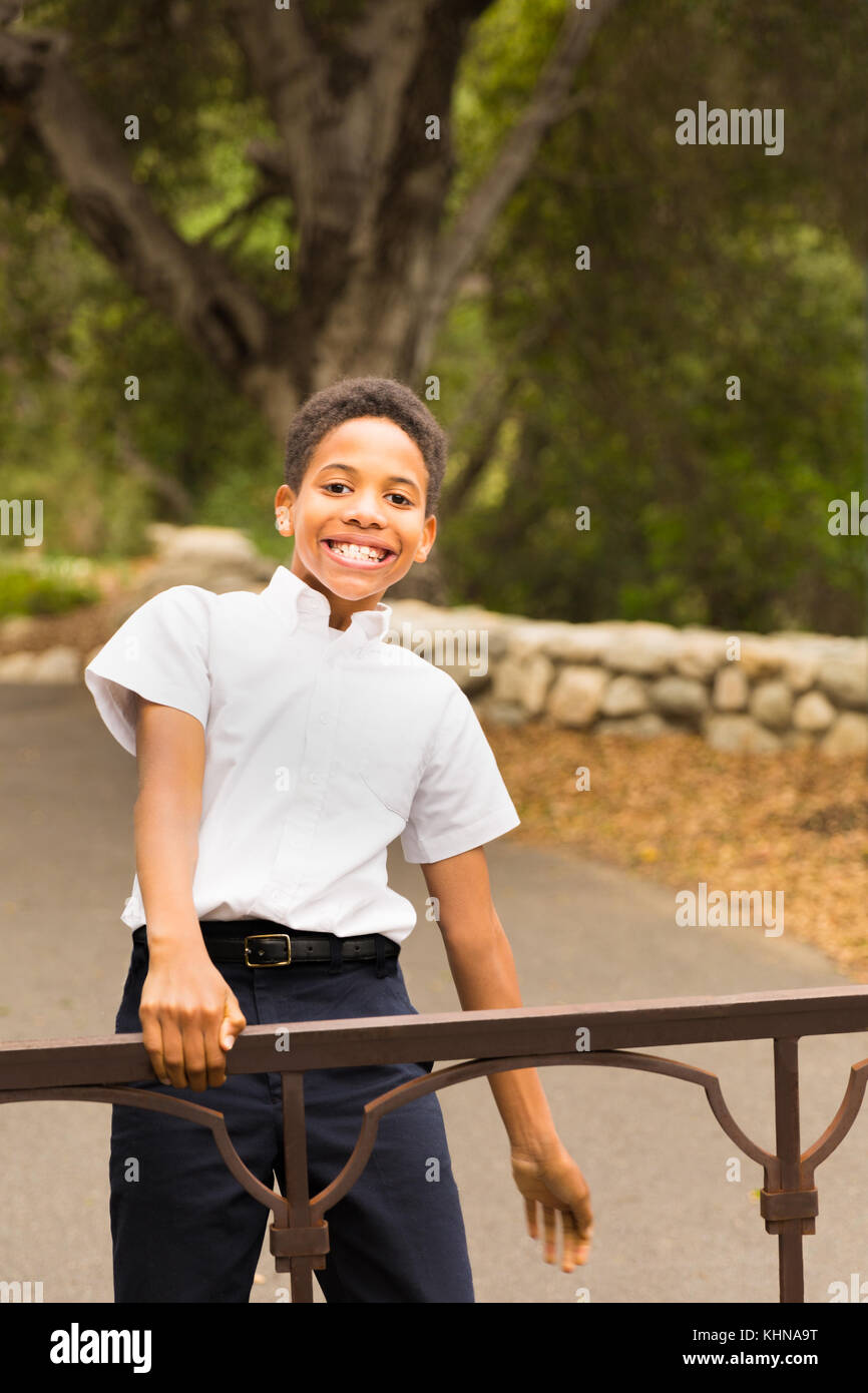 Happy African American boy standing, playing, or swinging on iron gate ...