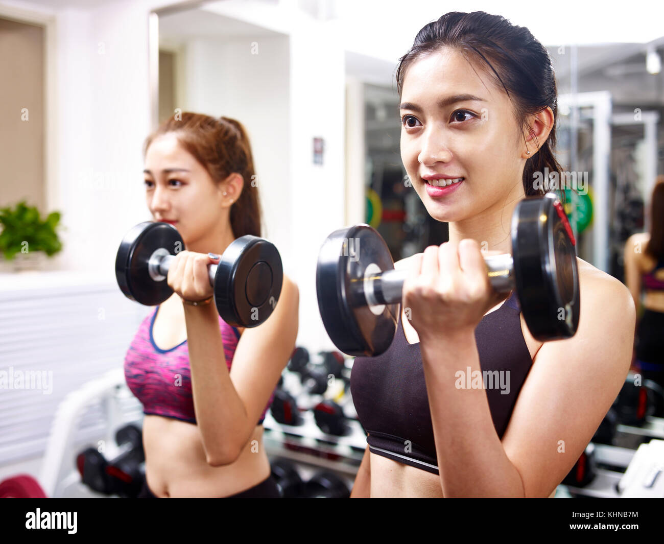 two young asian women working out exercising in gym using dumbbells ...