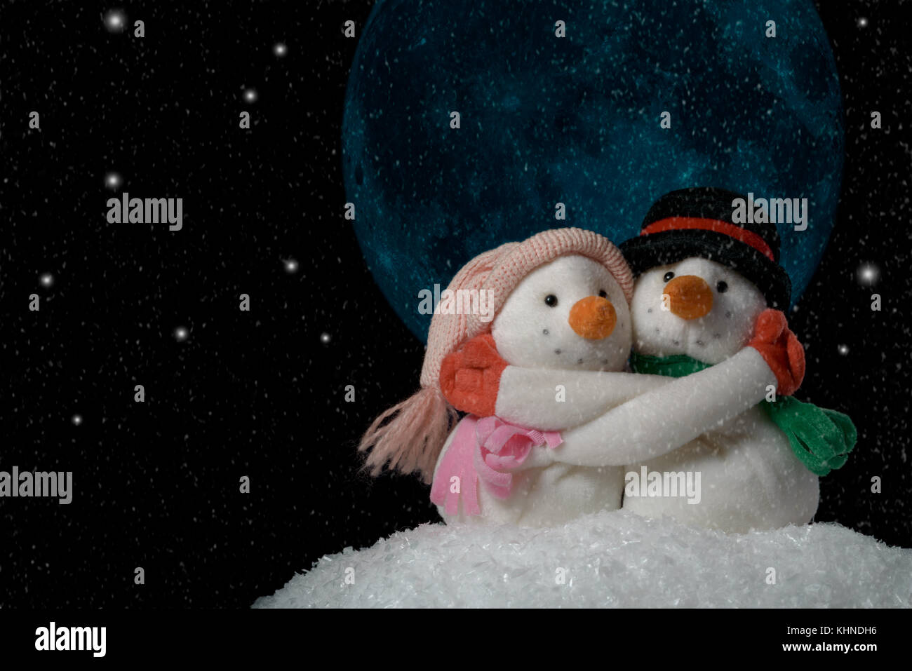 Cute snowmen toys on snow hugging each other against black sky and full ...