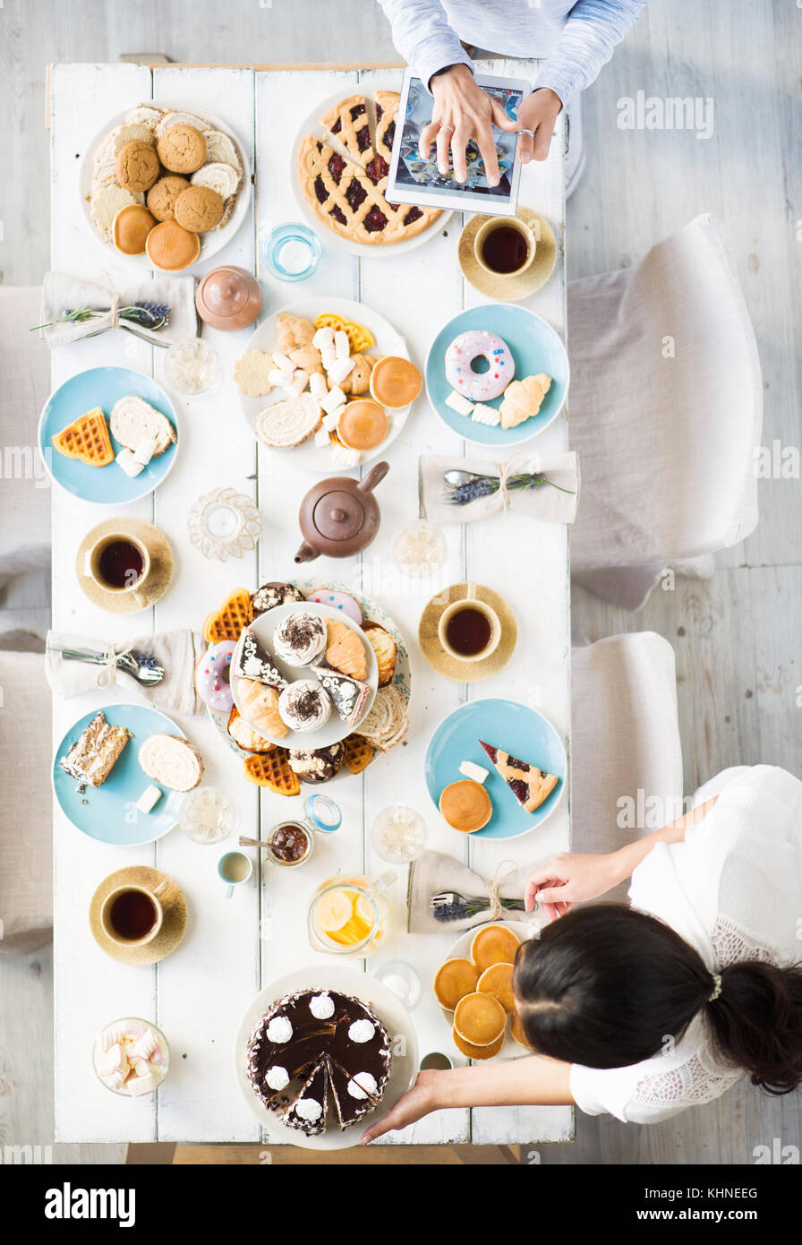 Girl serving table with homemade festive food while her friend with ...