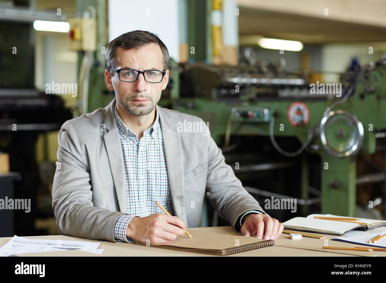 Serious engineer sketching in notepad by workplace on background of ...