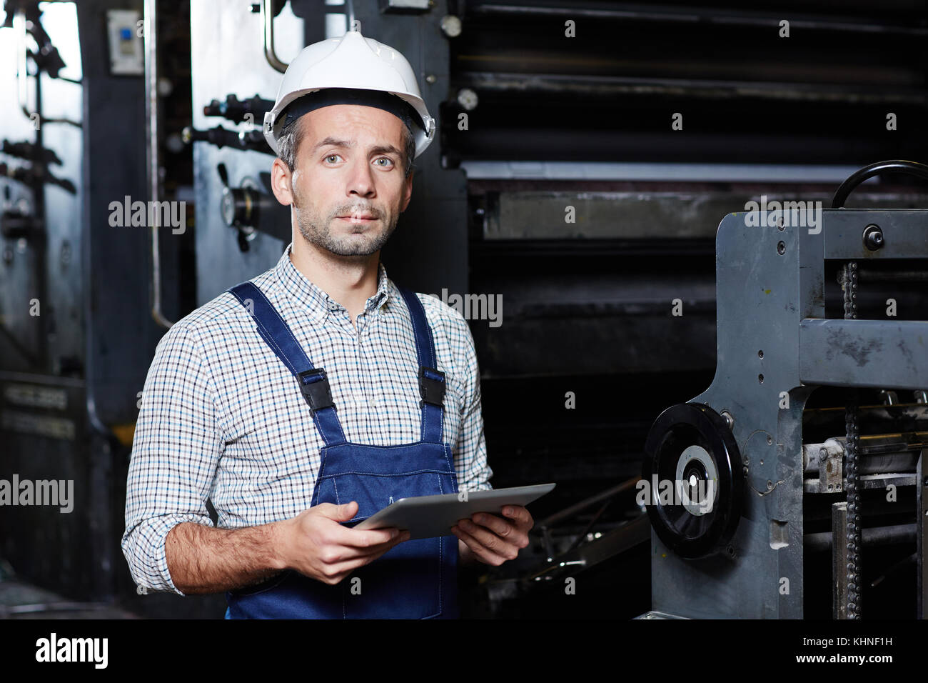 Worker with touchpad looking at camera while standing by industrial ...