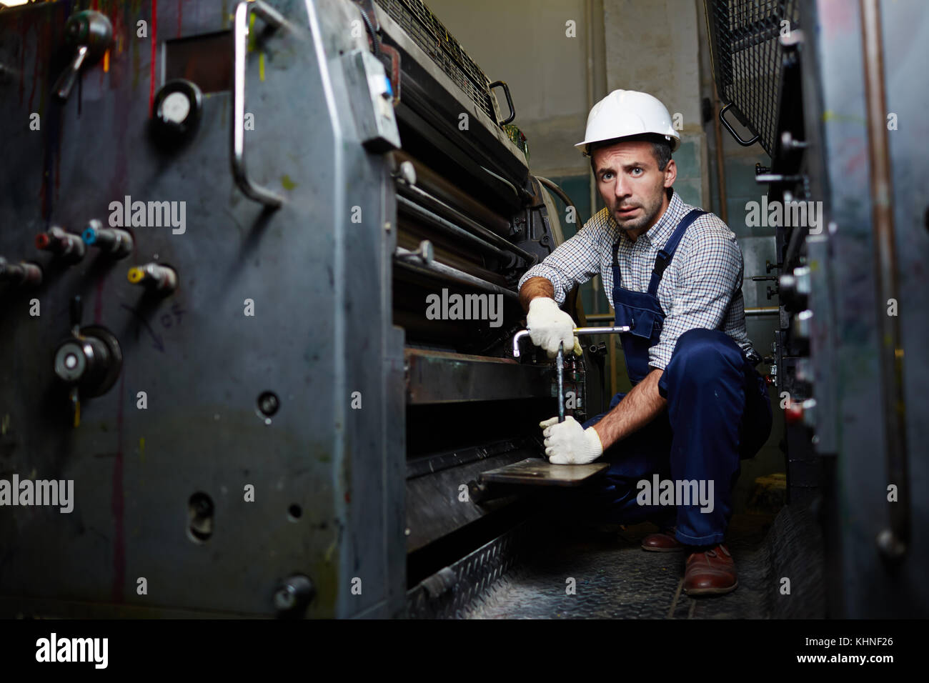 Engineer with handtool doing his work by huge industrial machine in ...