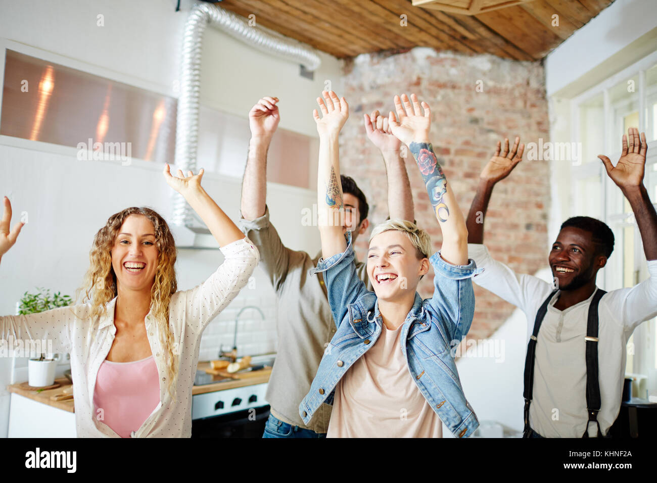 Ecstatic and laughing friends with raised hands dancing at party at ...