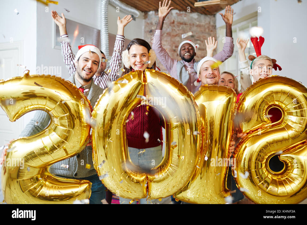 Friends with raised hands holding inflatable numbers in form of 2, 0, 1 ...