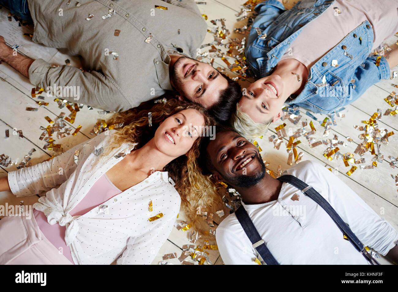 Four intercultural friends lying head to head on the floor covered with ...