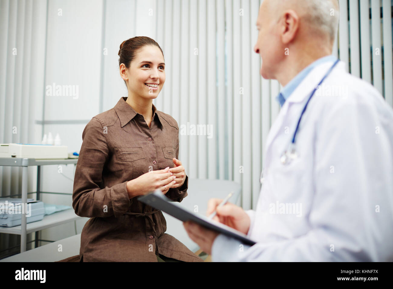 Happy young woman visiting doctor and listening to his advice during ...
