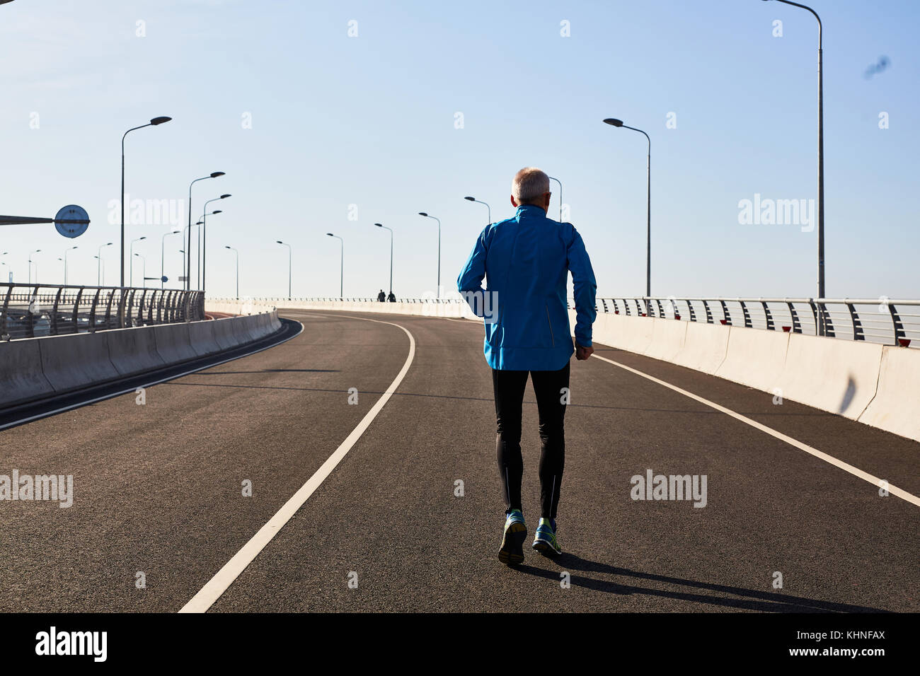 Rear view of man in leggins and sport jacket running along cycling ...