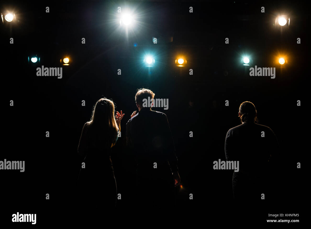 A rear view of three 3 student actors on stage in a theatre performing ...