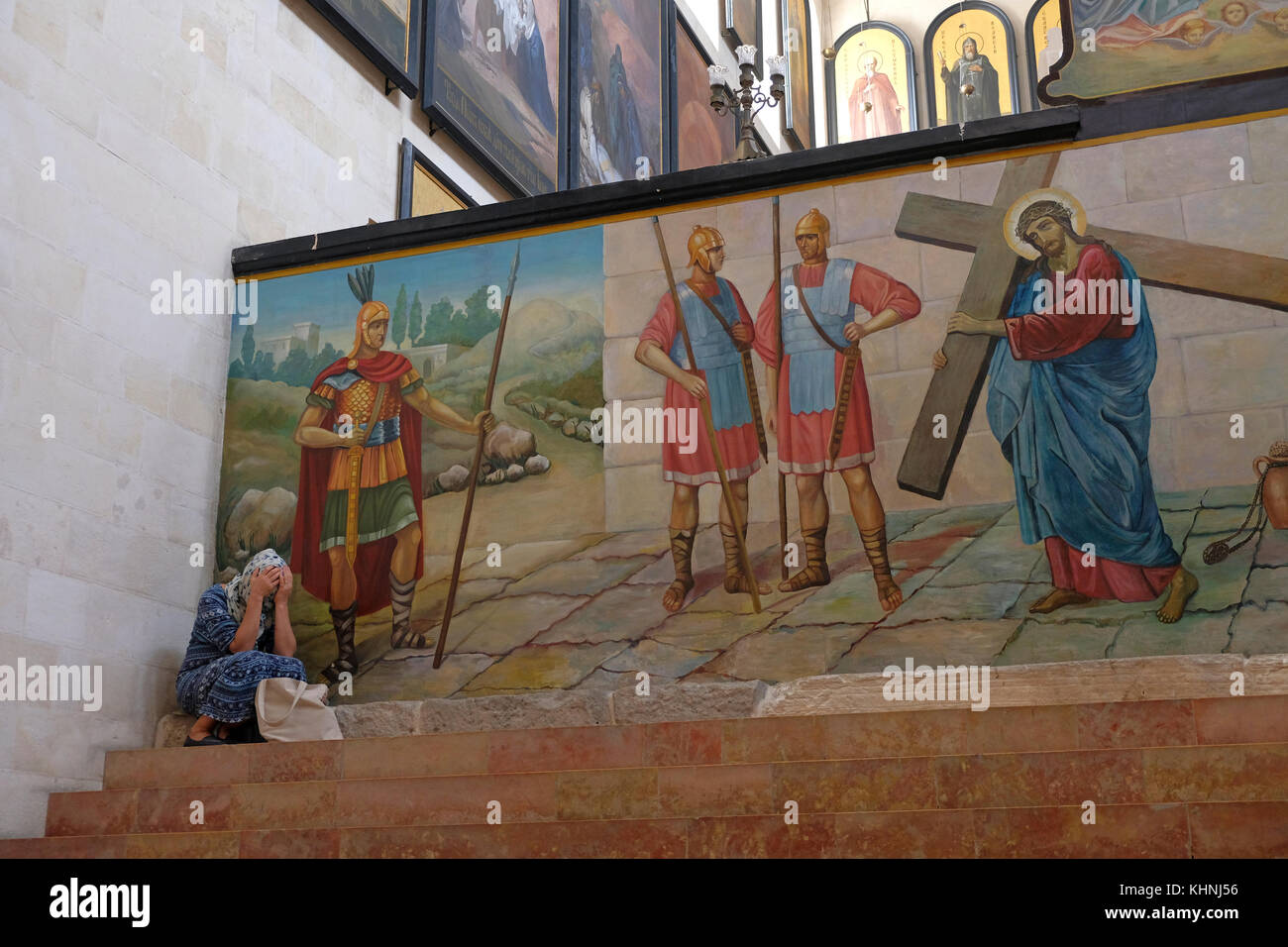 A Russian Orthodox pilgrim sits beneath a portrayal of Jesus carrying ...