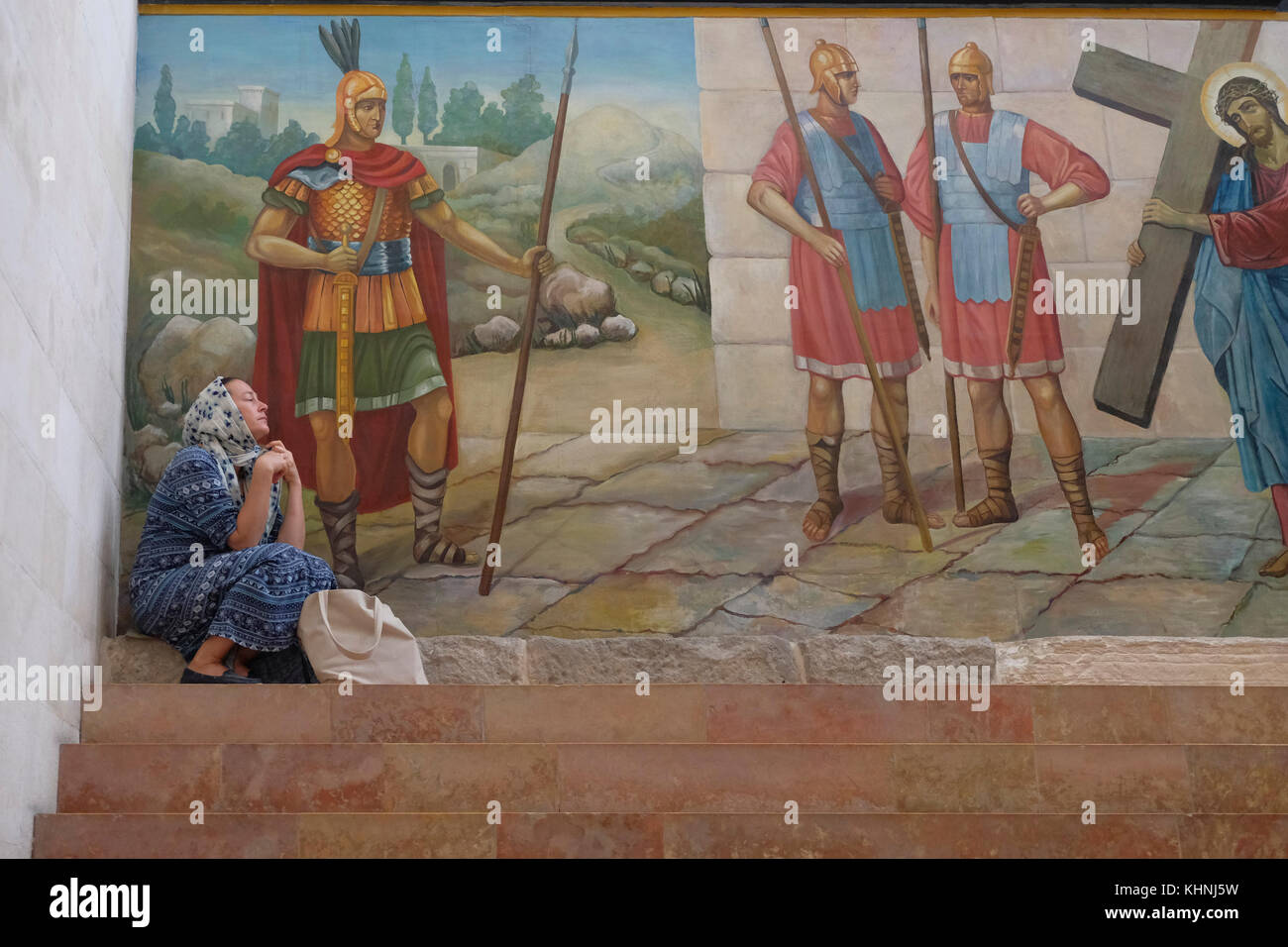 A Russian Orthodox pilgrim sits beneath a portrayal of Jesus carrying ...