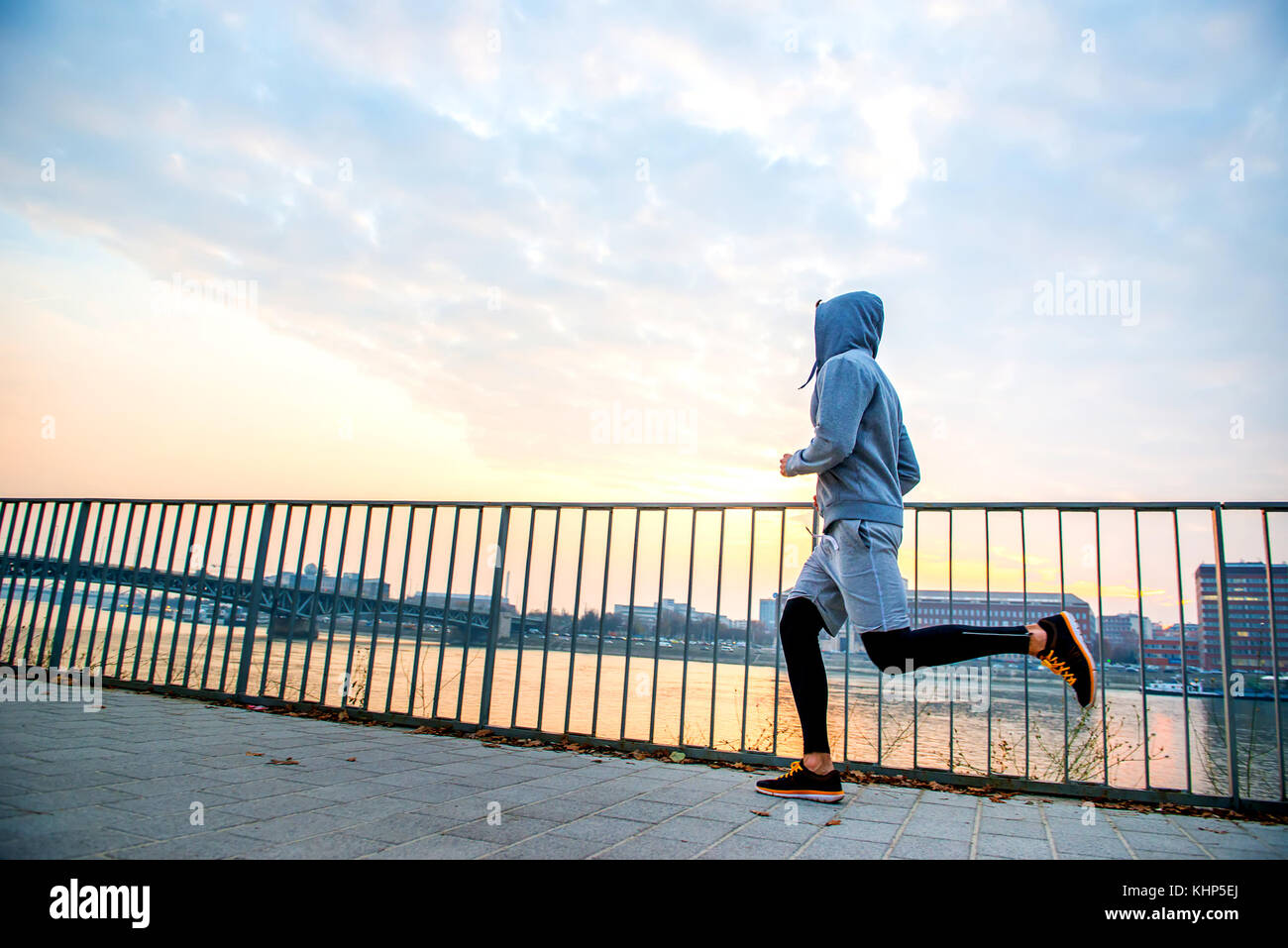 A handsome young man running in the sunset next to a fence on the ...