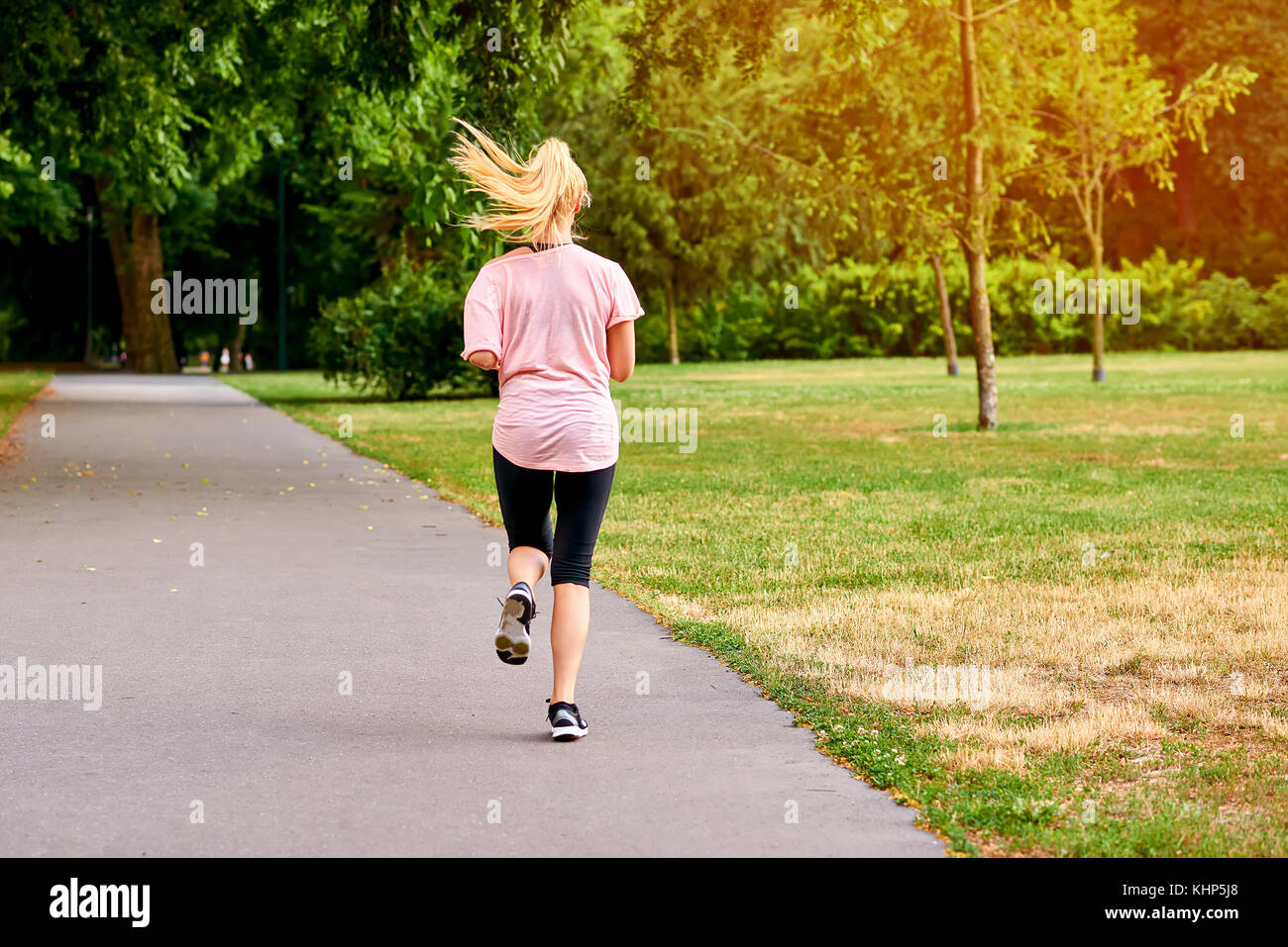 A beautiful young blonde woman running away from the camera on the road ...