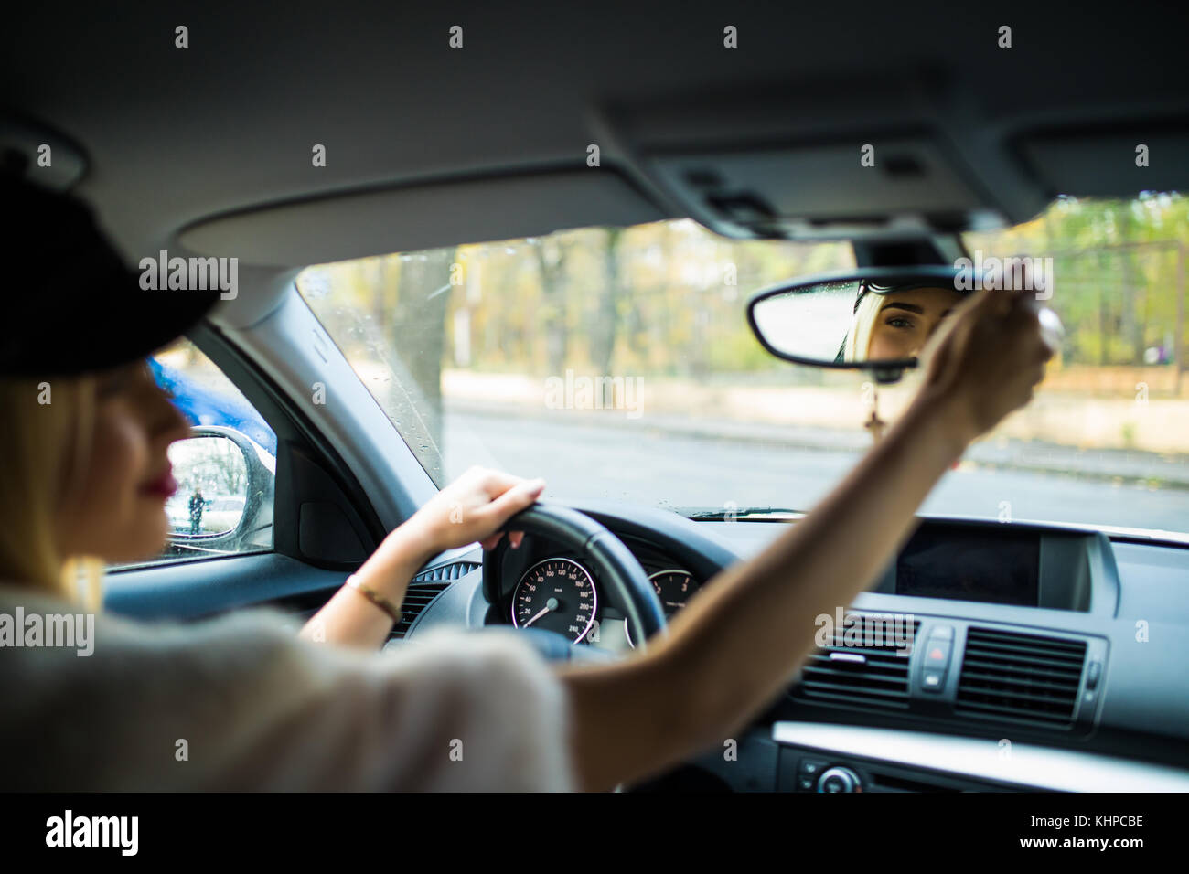 Happy young woman driver looking adjusting rear view car mirror, making ...
