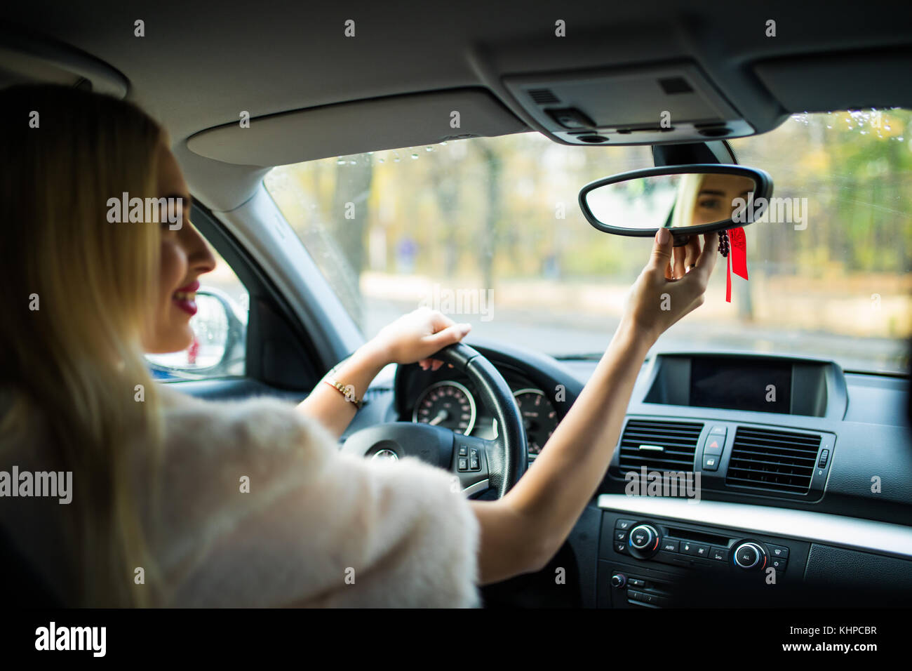 Happy young woman driver looking adjusting rear view car mirror, making ...