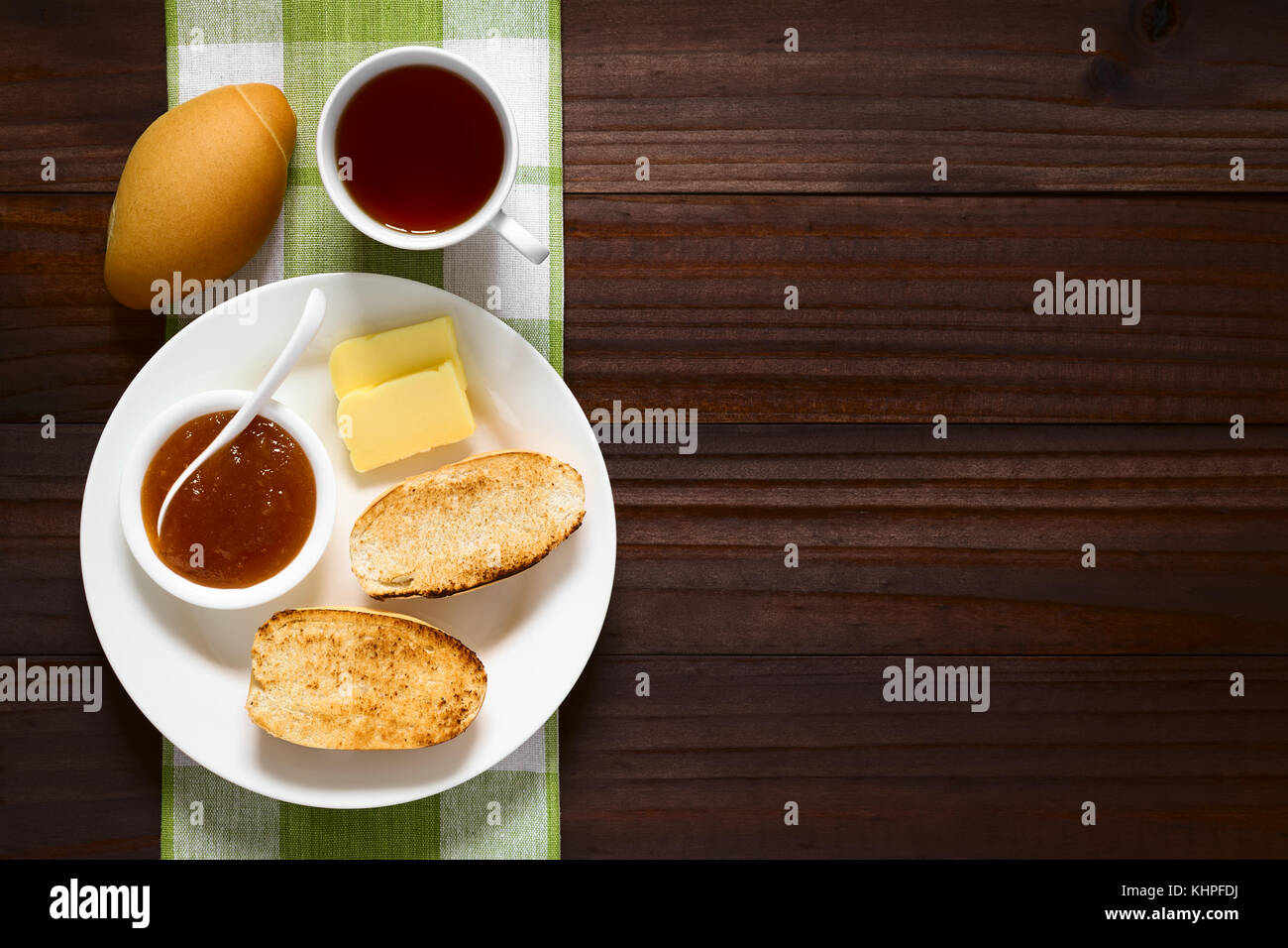 Toasted bread roll halves with butter, peach jam and tea on the side ...