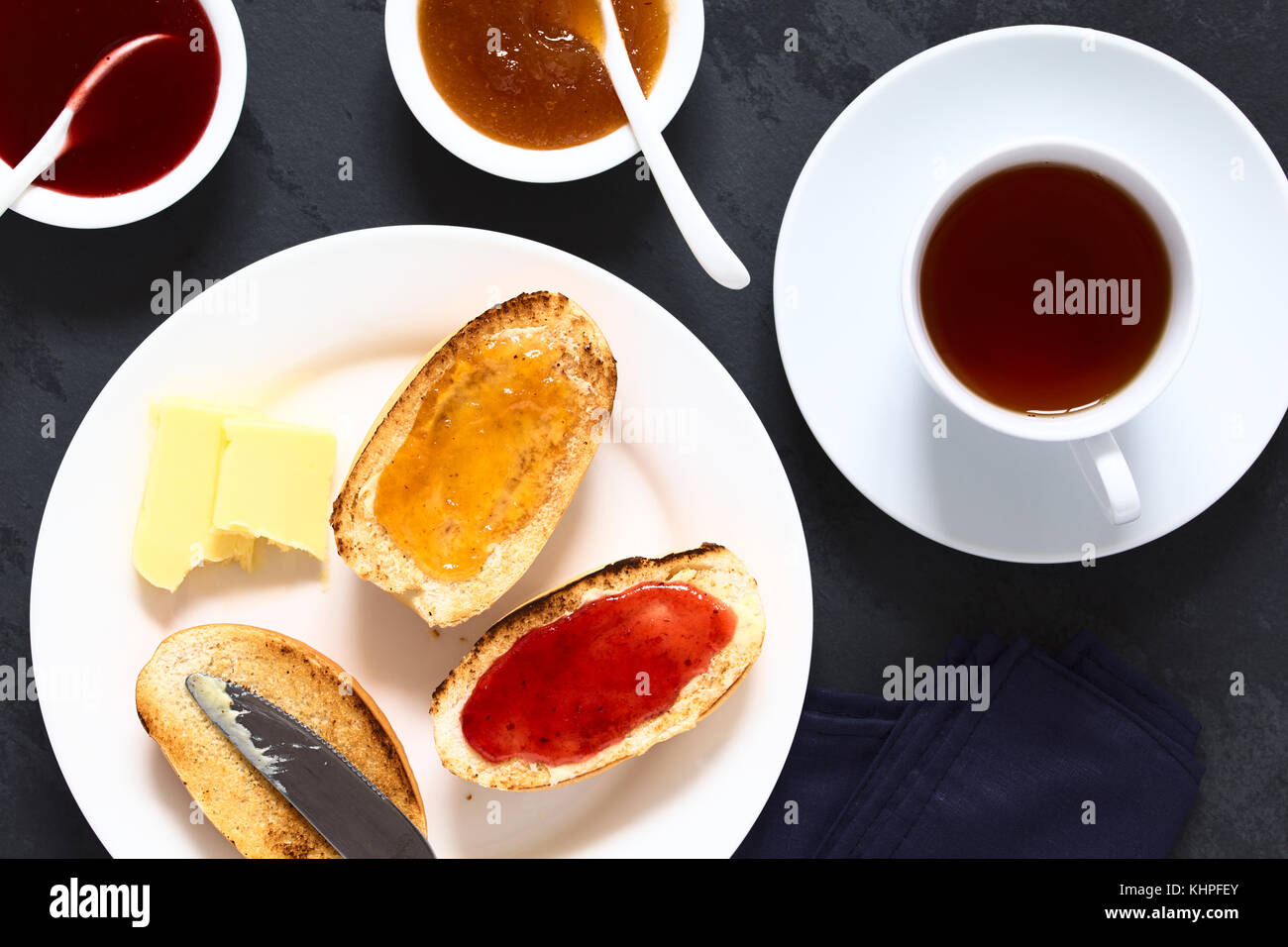 Toasted bread rolls with butter, peach and strawberry jam with tea on ...
