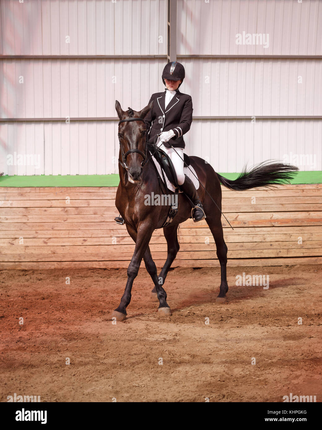 A sweet girl jockey rides a horse in a covered arena. Workout ...