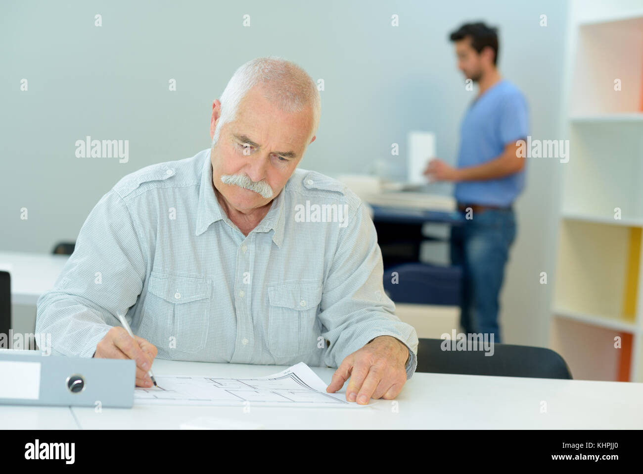 Senior man sat at desk filling out paperwork Stock Photo - Alamy