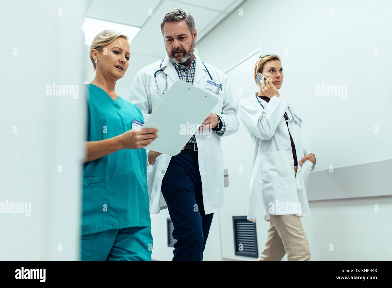 Busy hospital staff walking in hospital hallway discussing medical ...