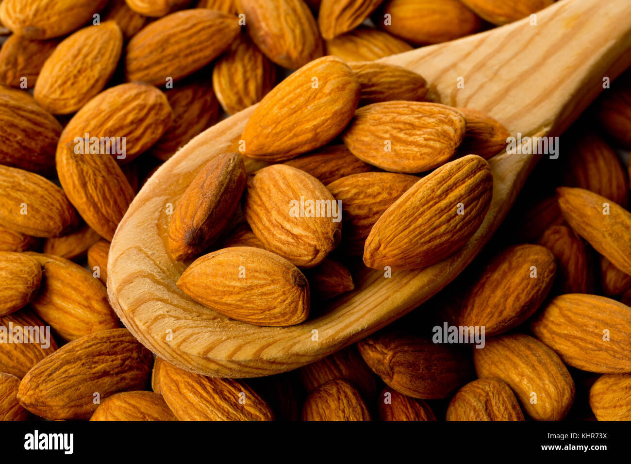 Heap of shelled almond kernels in wooden spoon on almond background ...