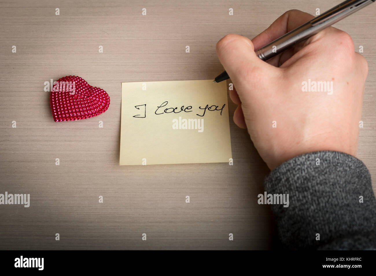 Man's hand writing I love you on sticky-note with little heart shaped ...