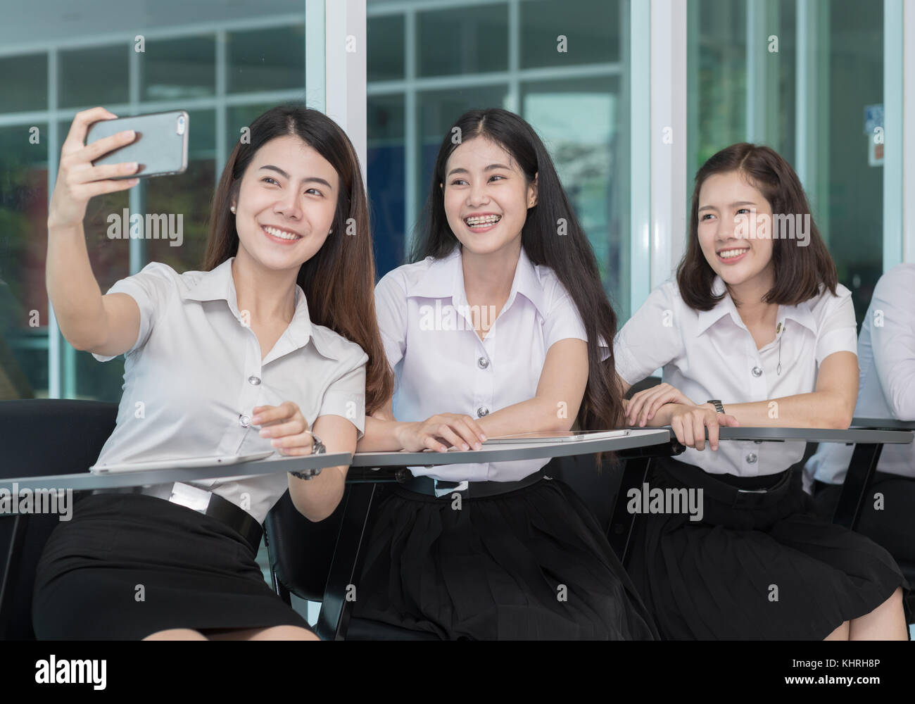 Cute asian young student in uniform sitting in a row to make funny ...