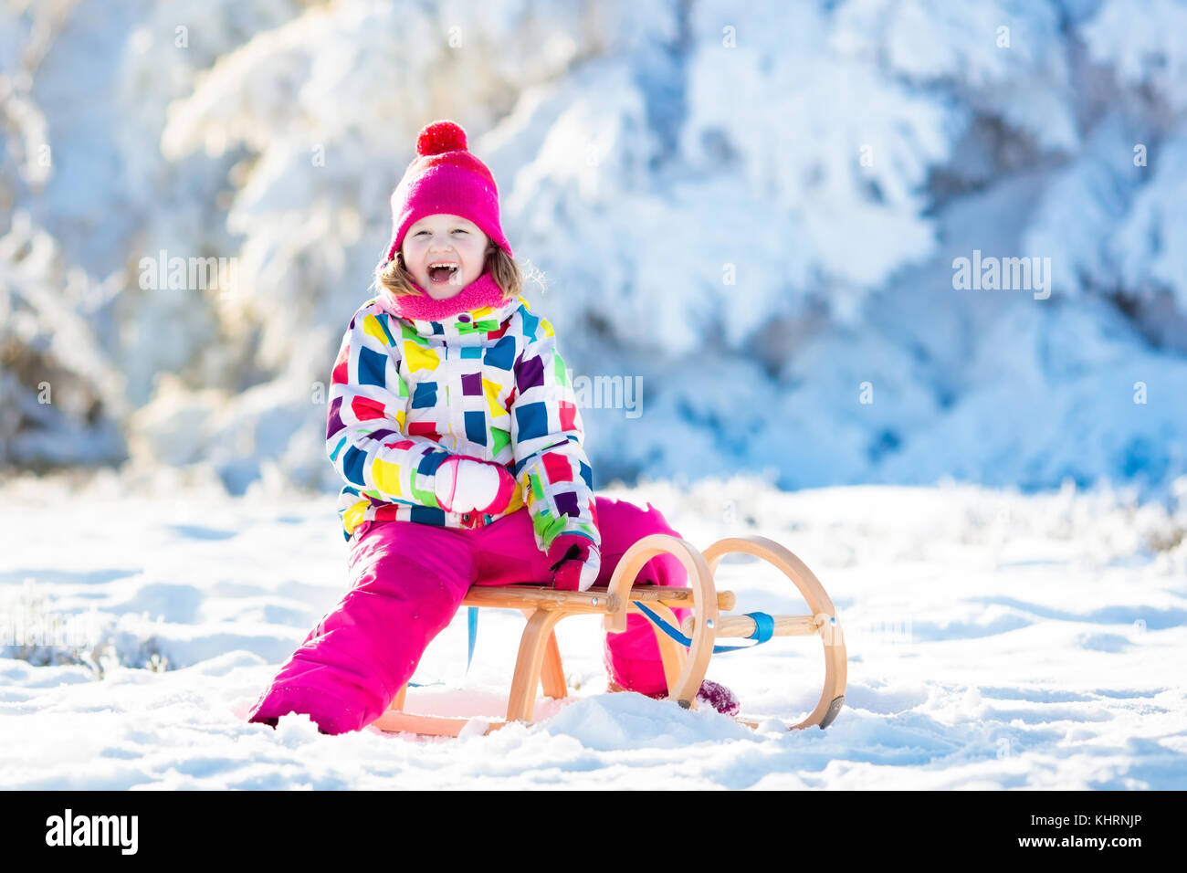 Little girl enjoying a sleigh ride. Child sledding. Toddler kid riding a sledge. Children play ...