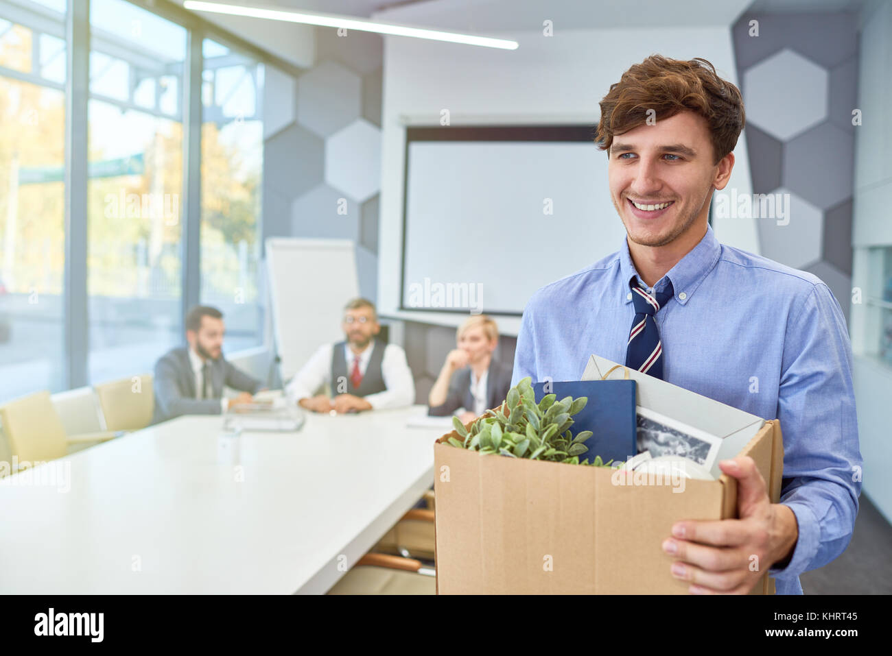 Portrait of smiling young man holding box of personal belongings being ...