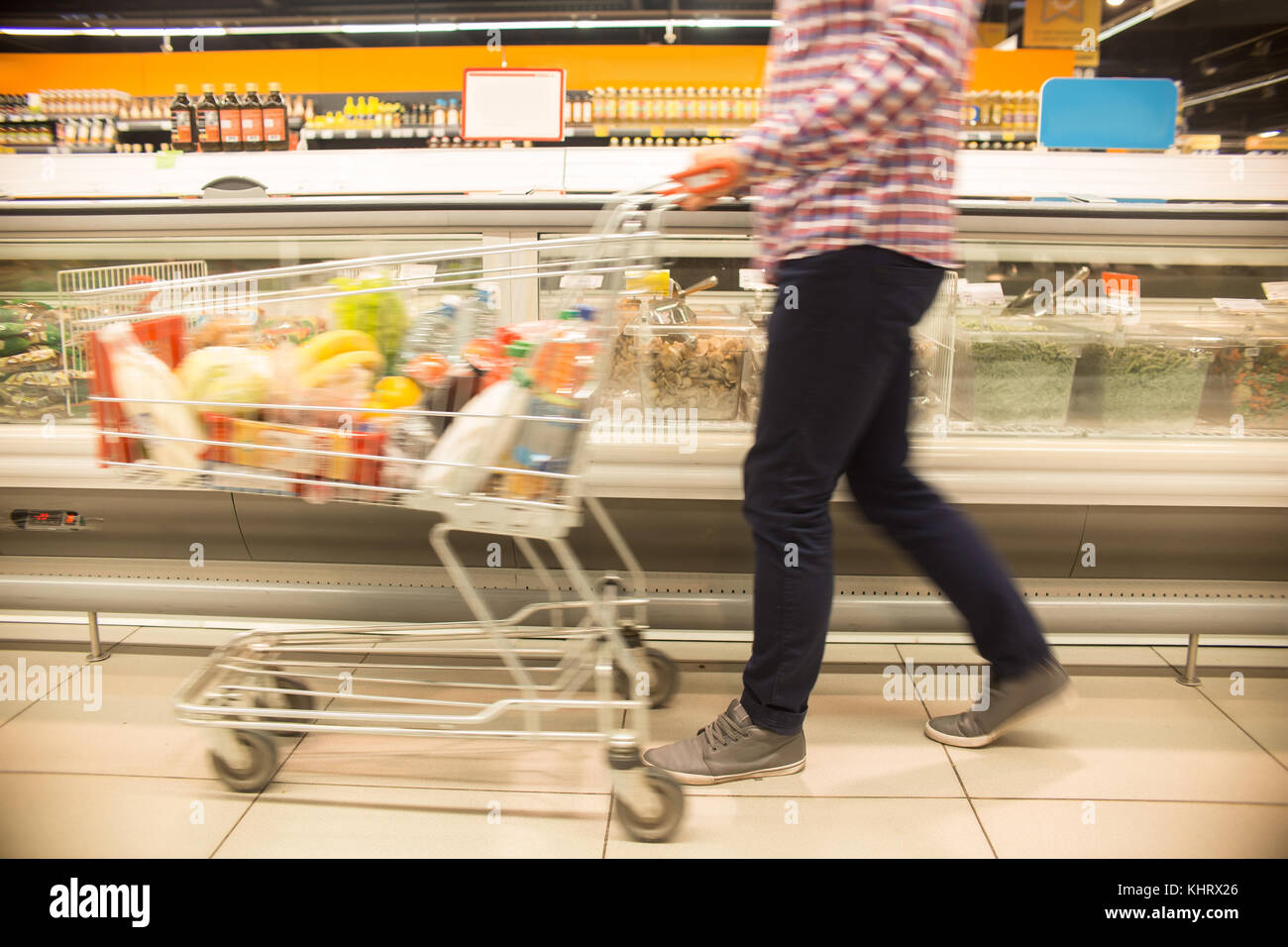 Low section view of unrecognizable man pushing shopping cart in blurred ...