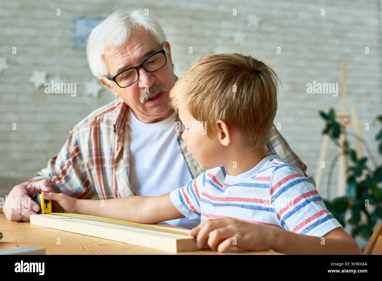 Portrait of grandfather and little boy talking while making wooden ...