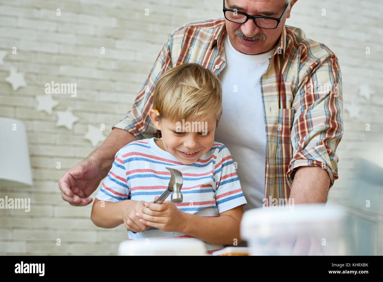 Portrait of smiling senior man helping little boy hammering nails while ...