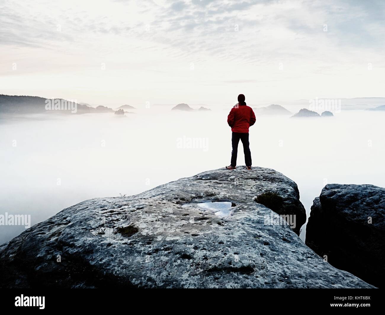 Rear view to traveler stand alone on cliff with mist bellow legs ...