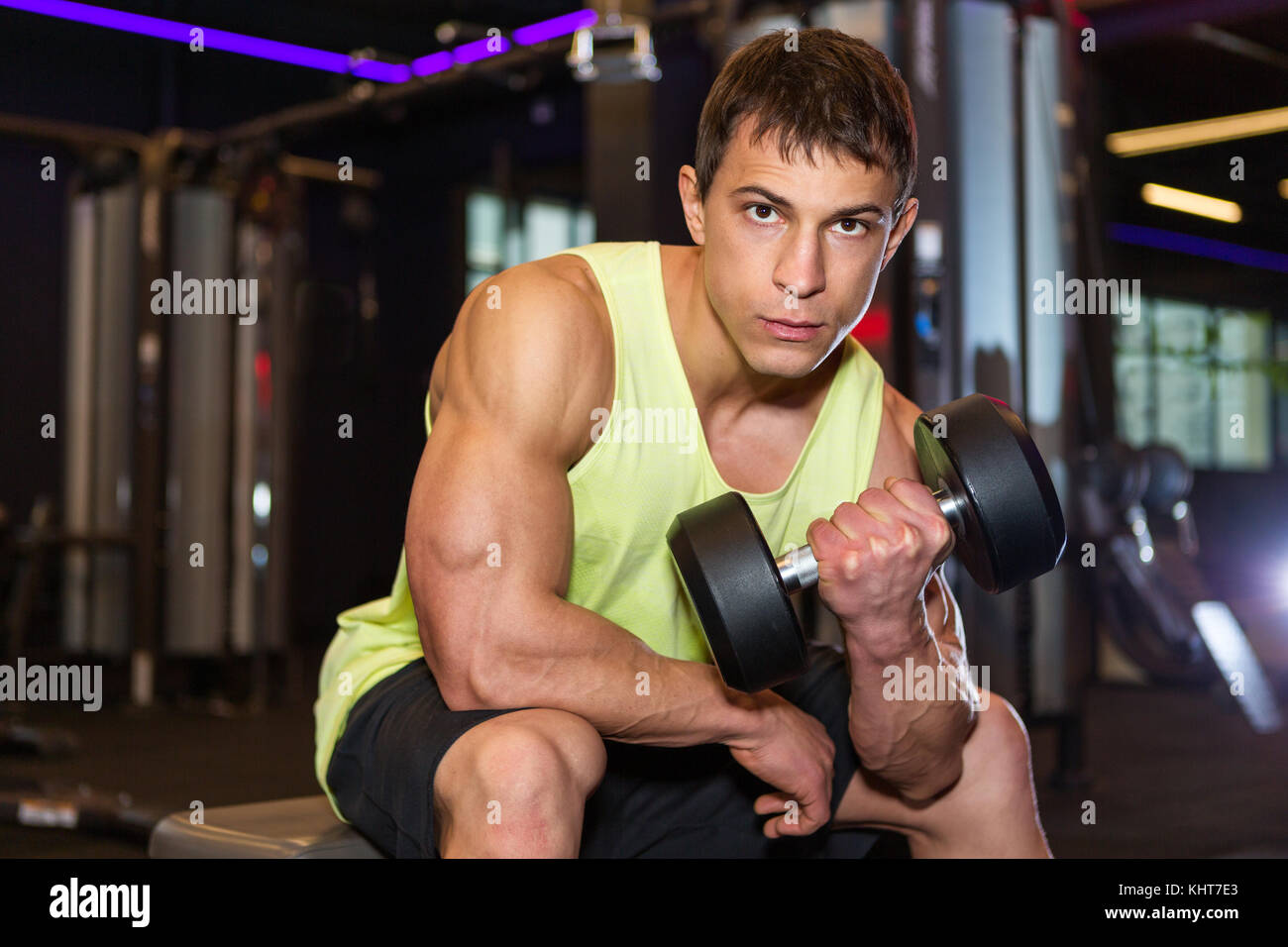 Young muscular man in a vest doing one-arm dumbbell rows on bench in ...