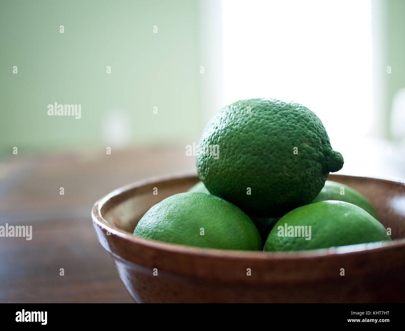 Limes in an earthen pottery bowl on wood table Stock Photo - Alamy