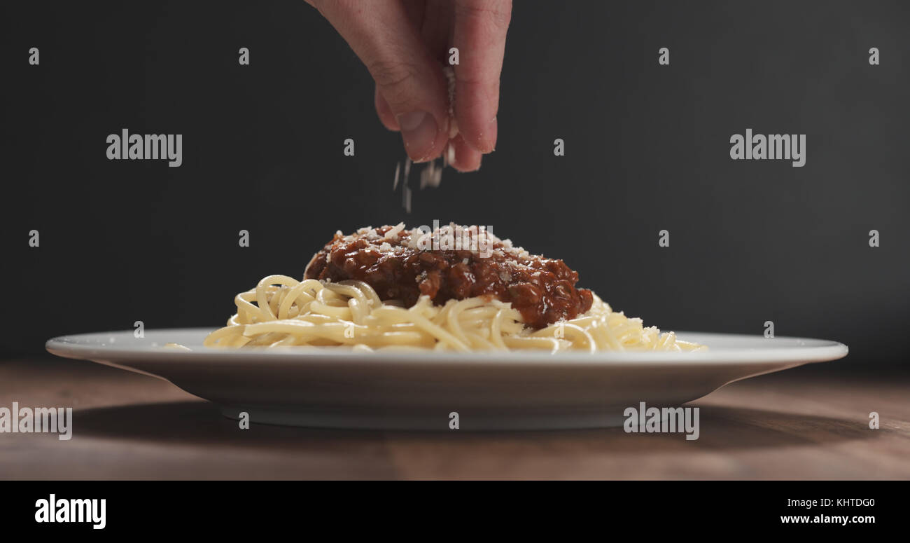 man hand sprinkle grated aged parmesan cheese over spaghetti bolognese ...