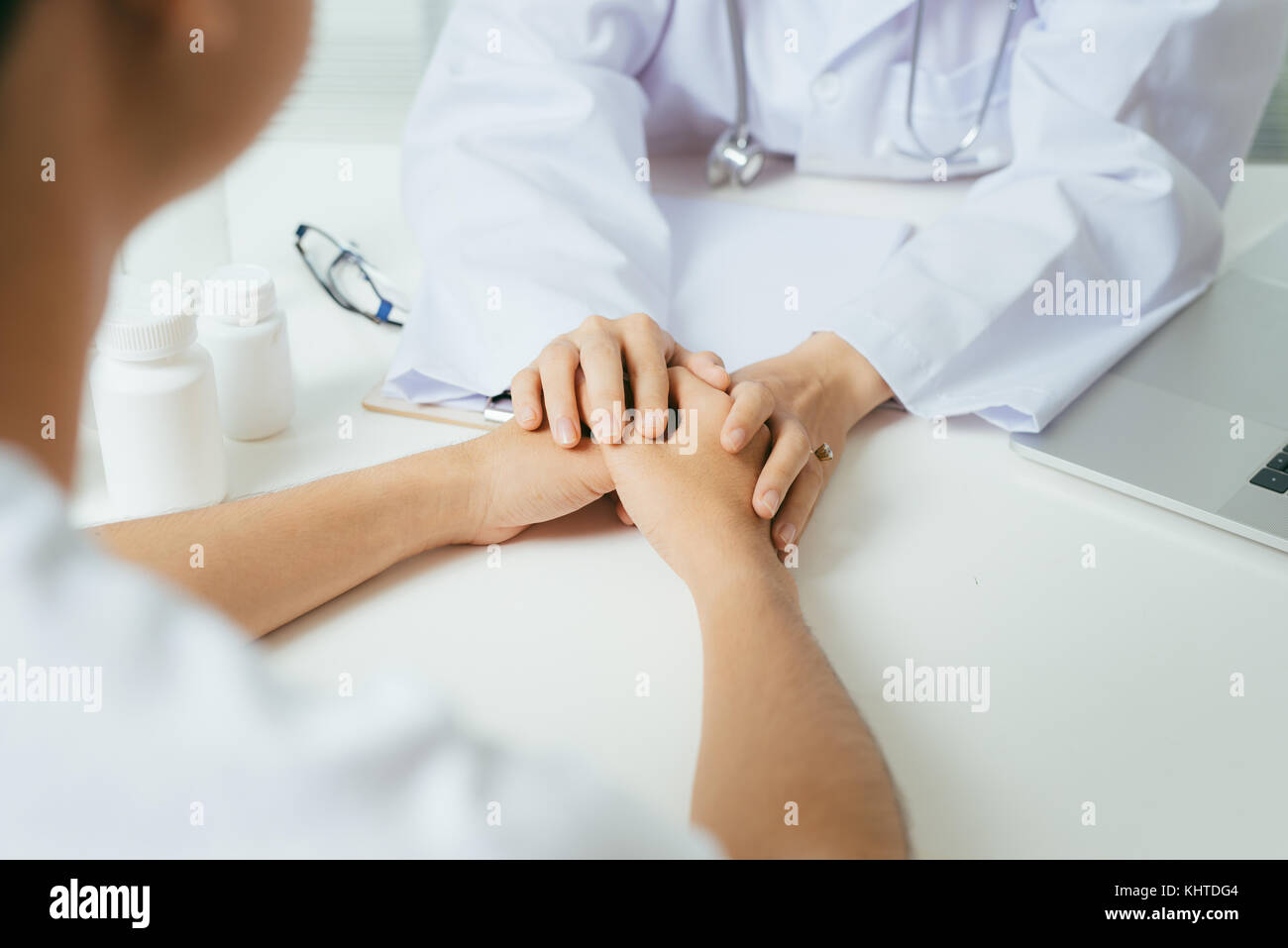 Friendly female doctor hands holding patient hand sitting at the desk ...
