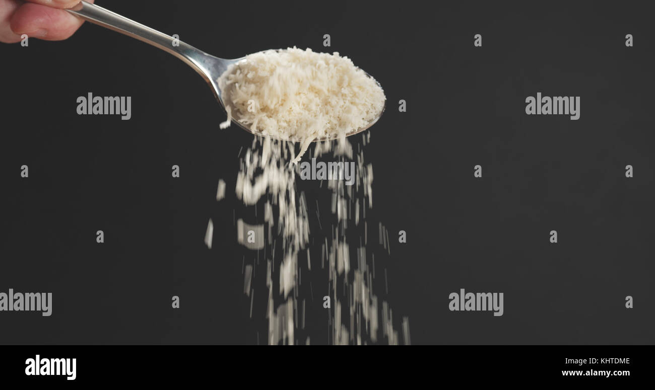 closeup of grated aged parmesan falling from spoon over dark background ...